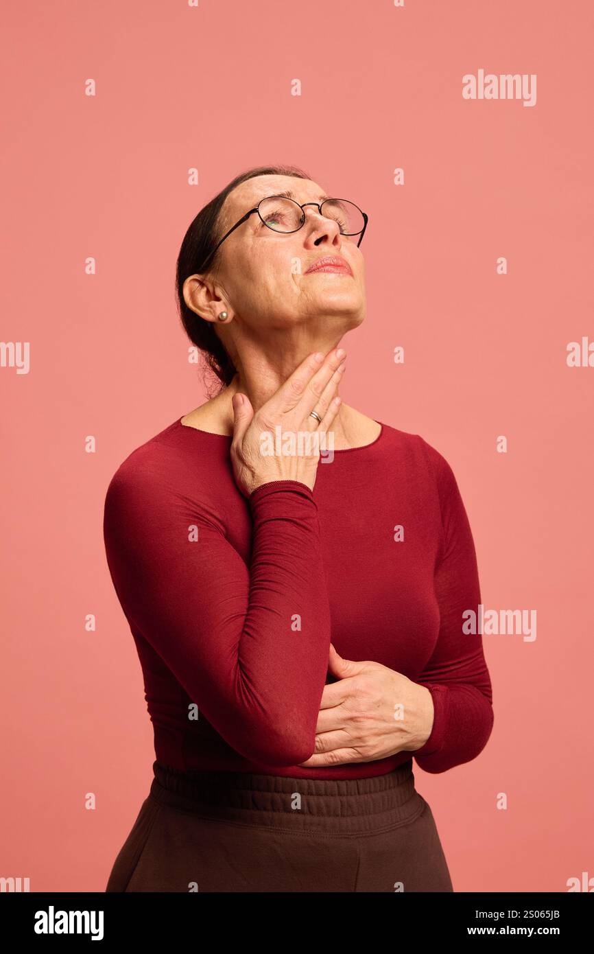 Woman in burgundy top touching neck with one hand, looking upward her ...