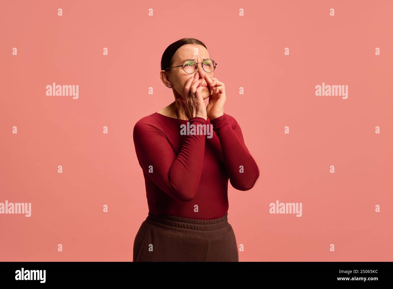 Woman in burgundy top holding nose bridge with both hands, squinting ...