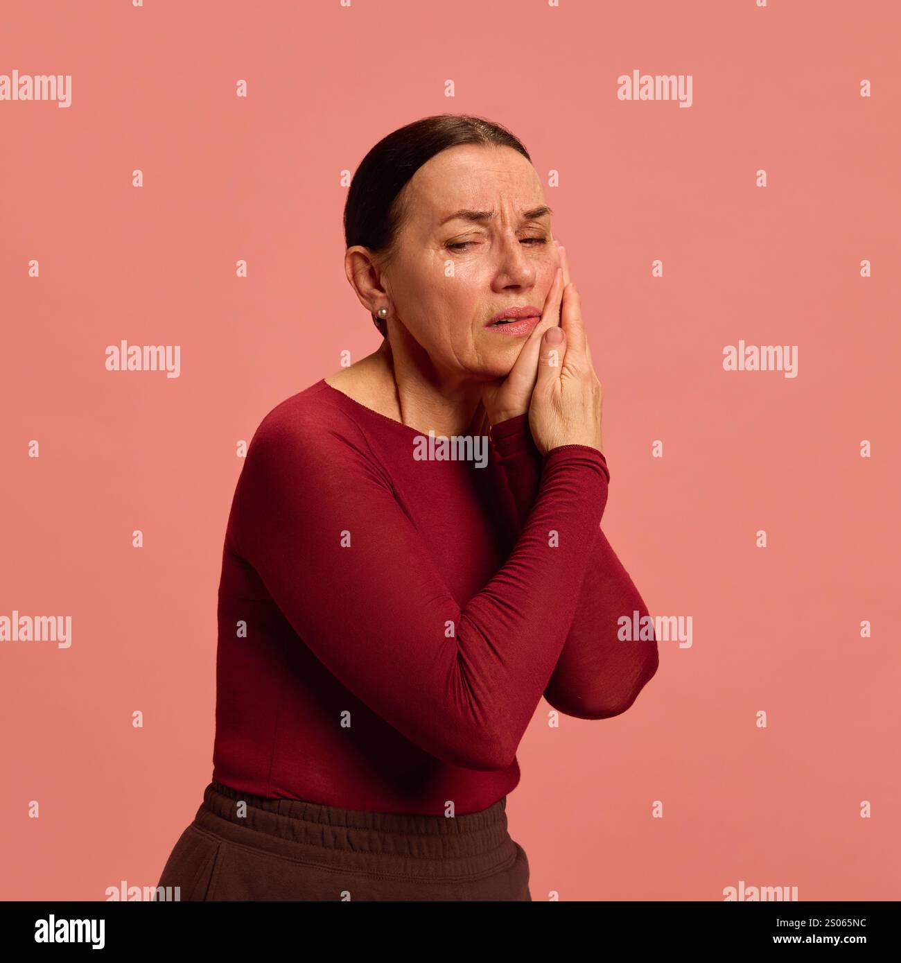 Elderly woman in red presses her cheek with both hands, showing ...