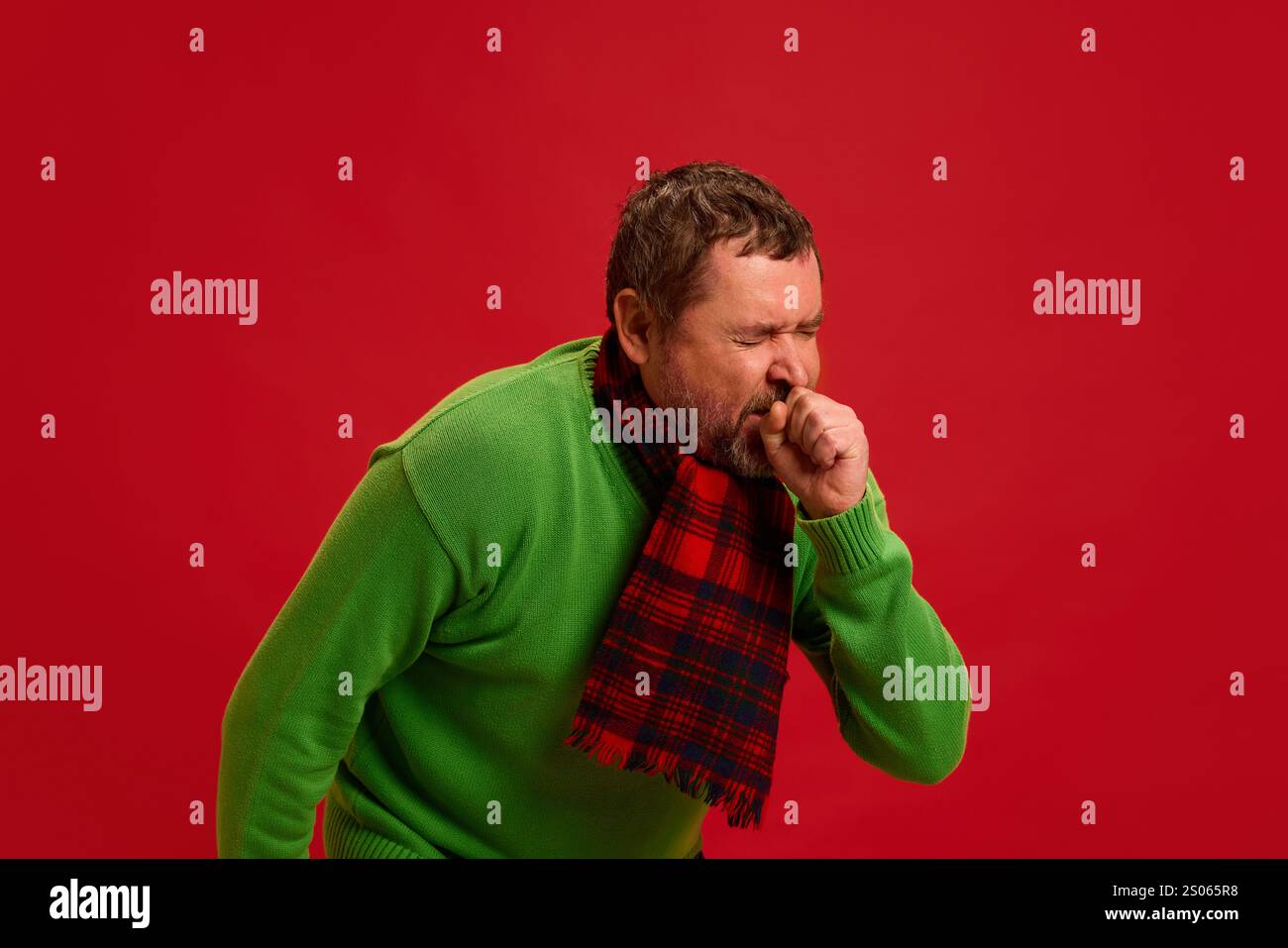 Man coughing into fist, wrapped in red scarf, face tense, showing ...