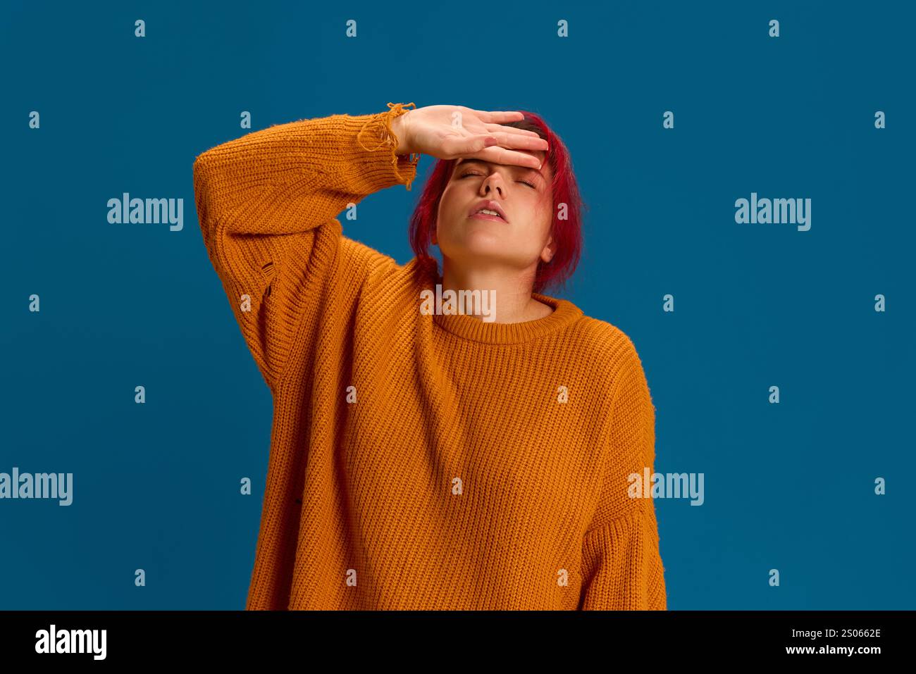 Portrait of young Caucasian woman holding forehead against deep blue ...