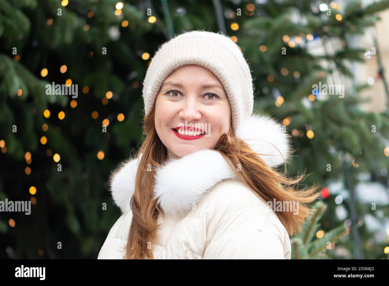 A smiling 30-35 year old woman stands near a decorated Christmas tree ...