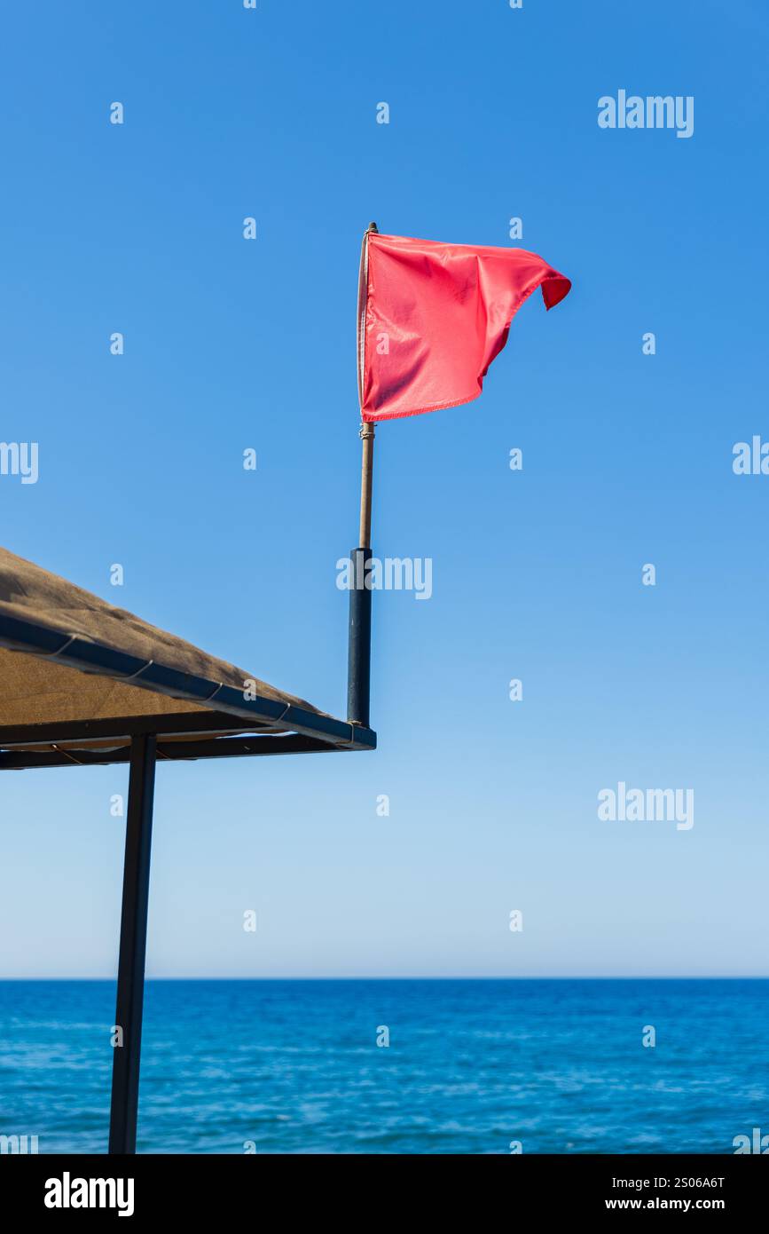 Red warning flag is waving on strong wind under blue sky on the beach ...