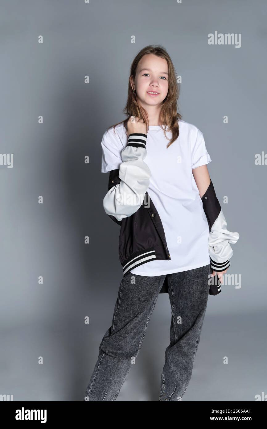 The young girl holds her jacket in a laid-back manner, eyes cast down ...