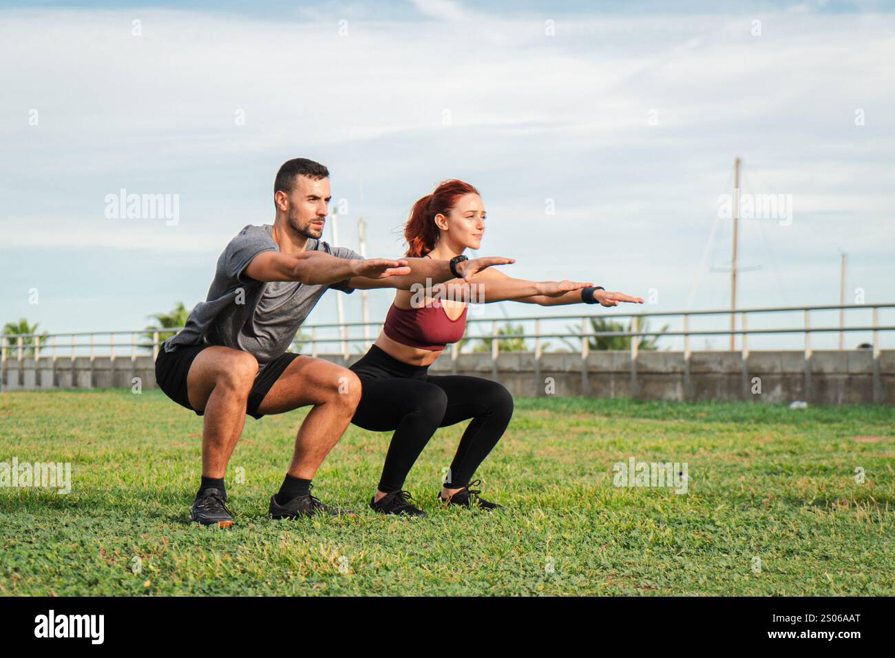 A fit couple performing squats together outdoors on a grassy field ...