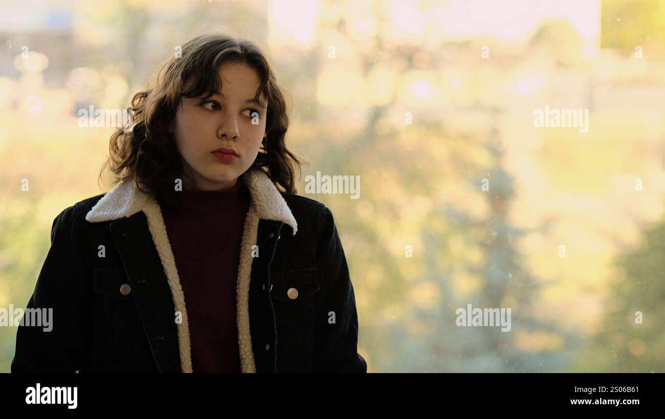 A young girl gazes outside, her posture relaxed but reflective. This ...