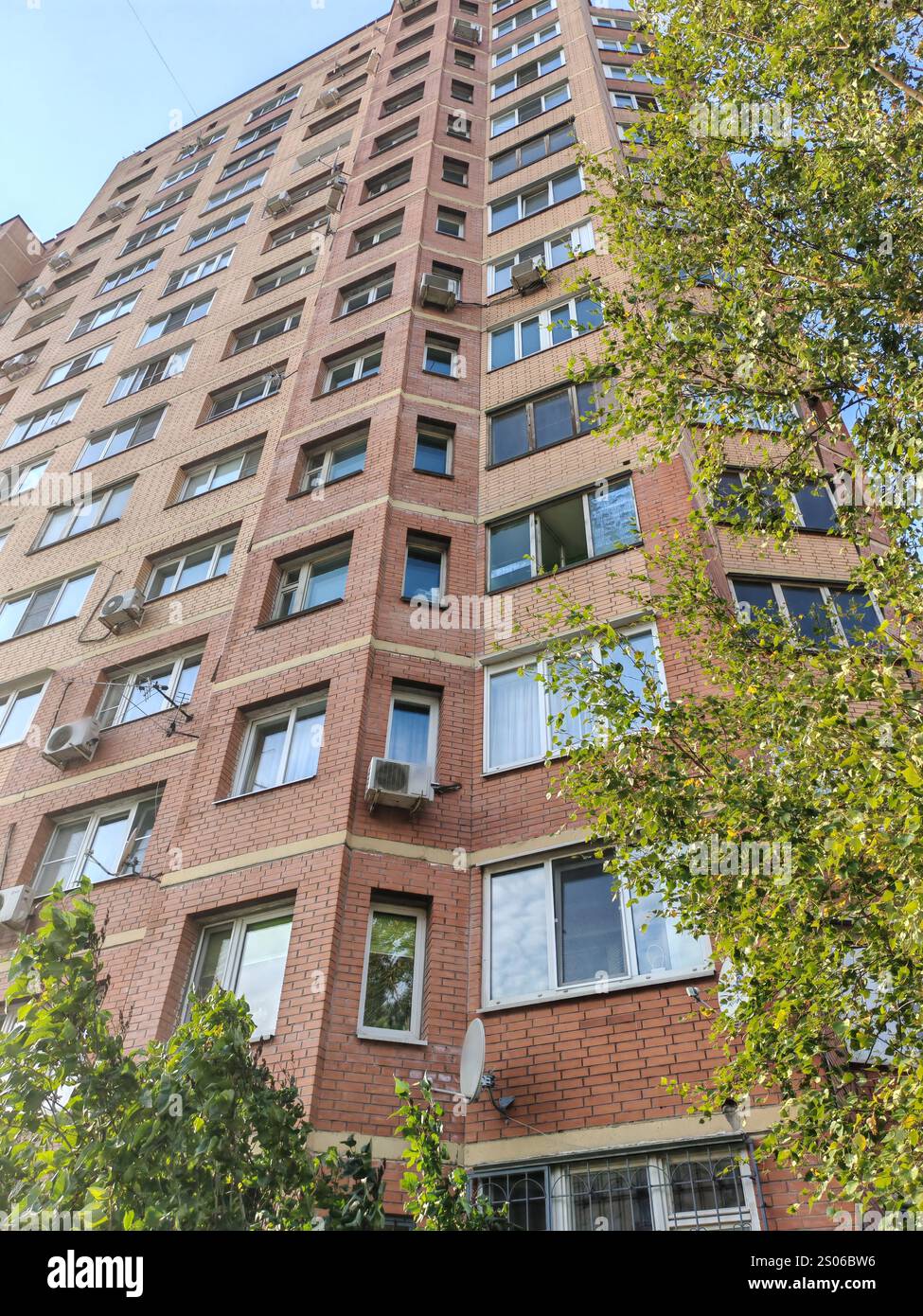 A tall red and beige brick residential building with multiple balconies ...