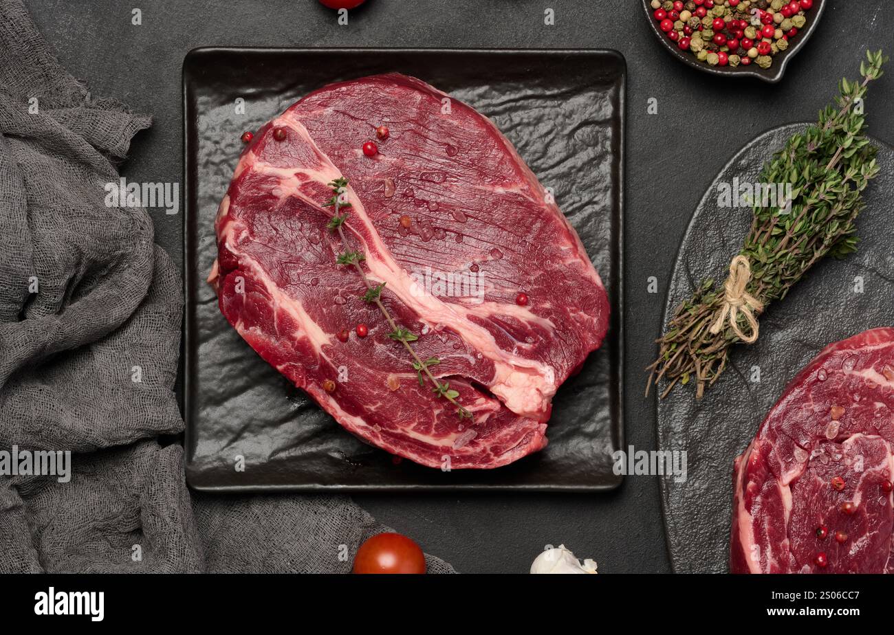 Raw chuck eye roll beef steak on black board, peppercorns, and sprigs ...