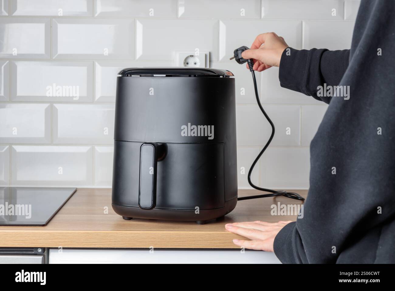 Woman at home using trendy kitchen gadget, air fryer, plugging in small ...