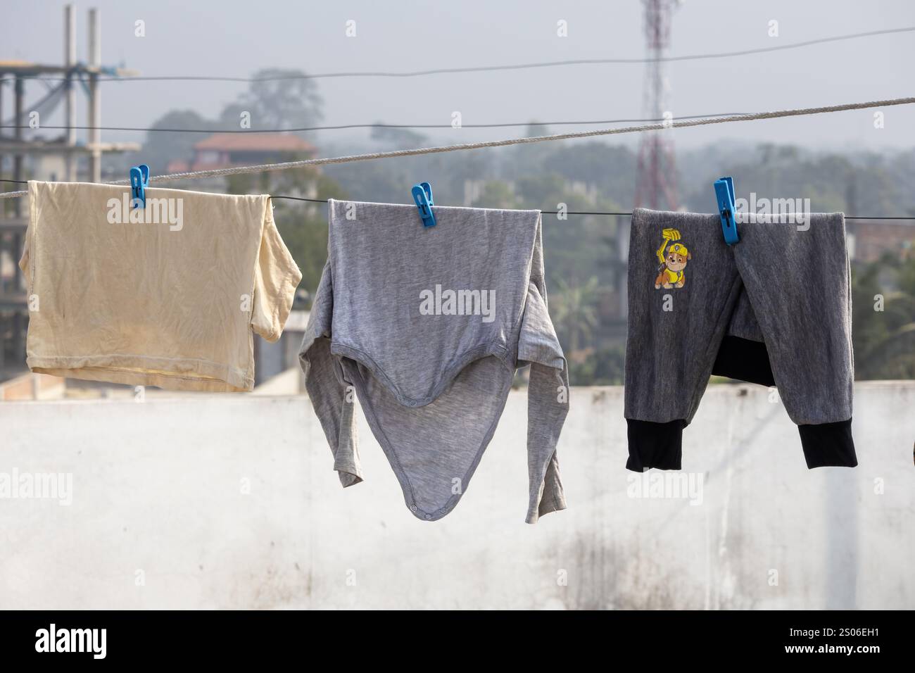 Wet baby clothes are hanging on a clothesline with clothespins on a ...