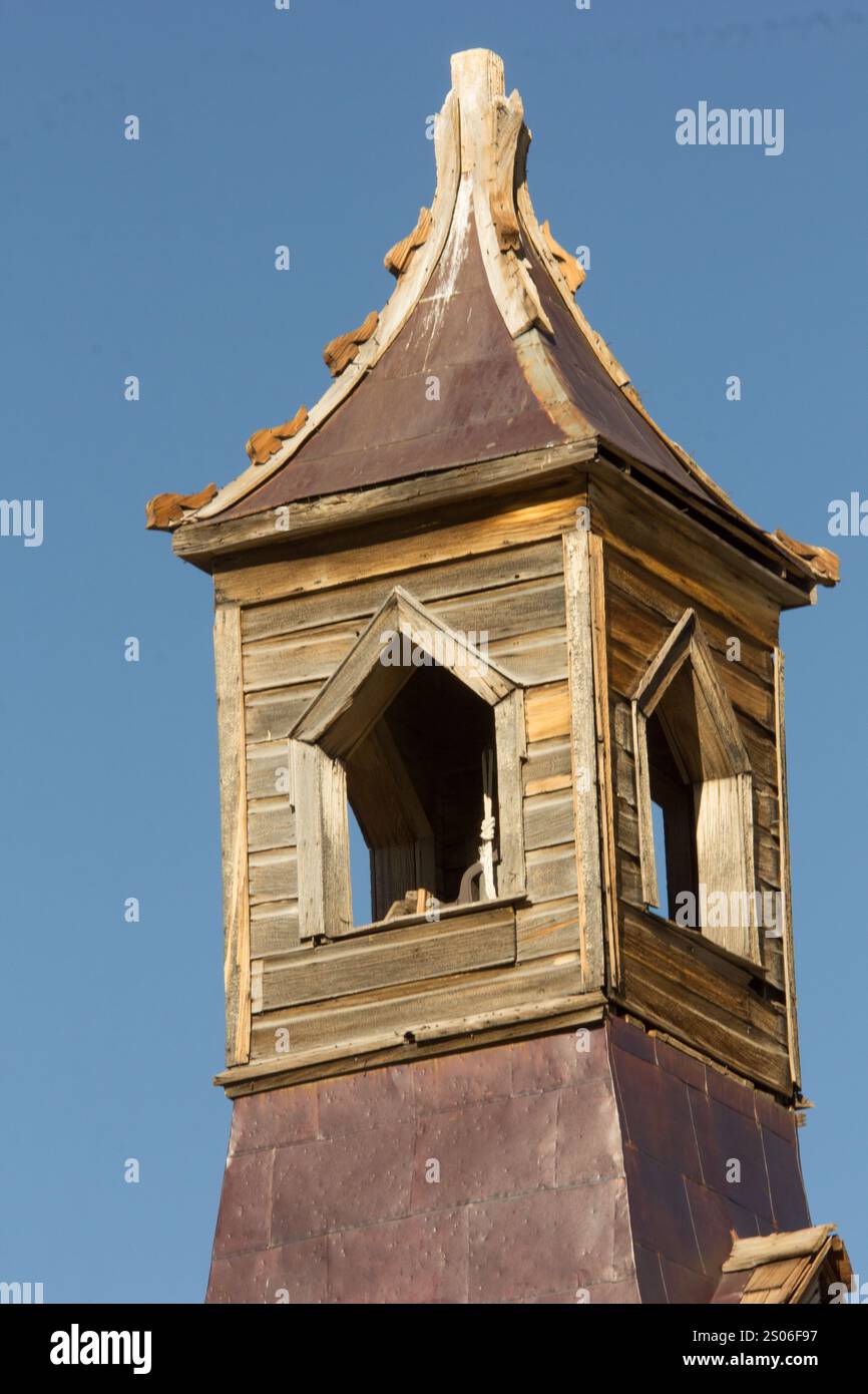 A small, old building with a steeple and a bell. The building is made ...