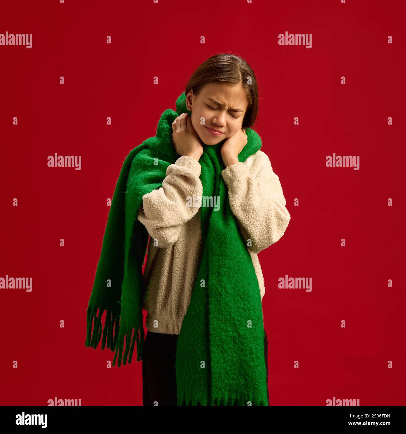 Teen girl in green scarf and beige sweater holding her throat in pain ...