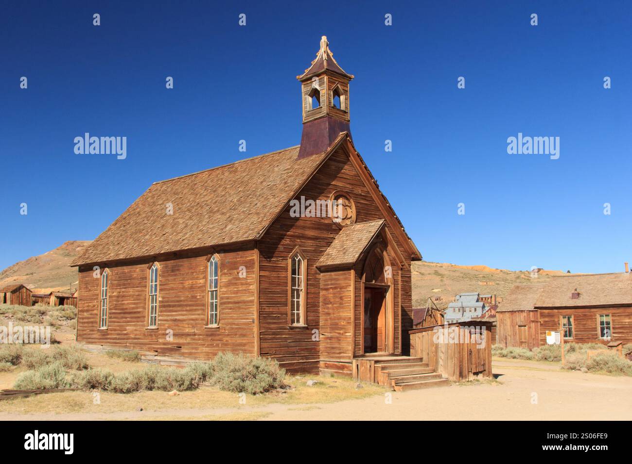 A small church with a steeple sits in a desert. The church is ...