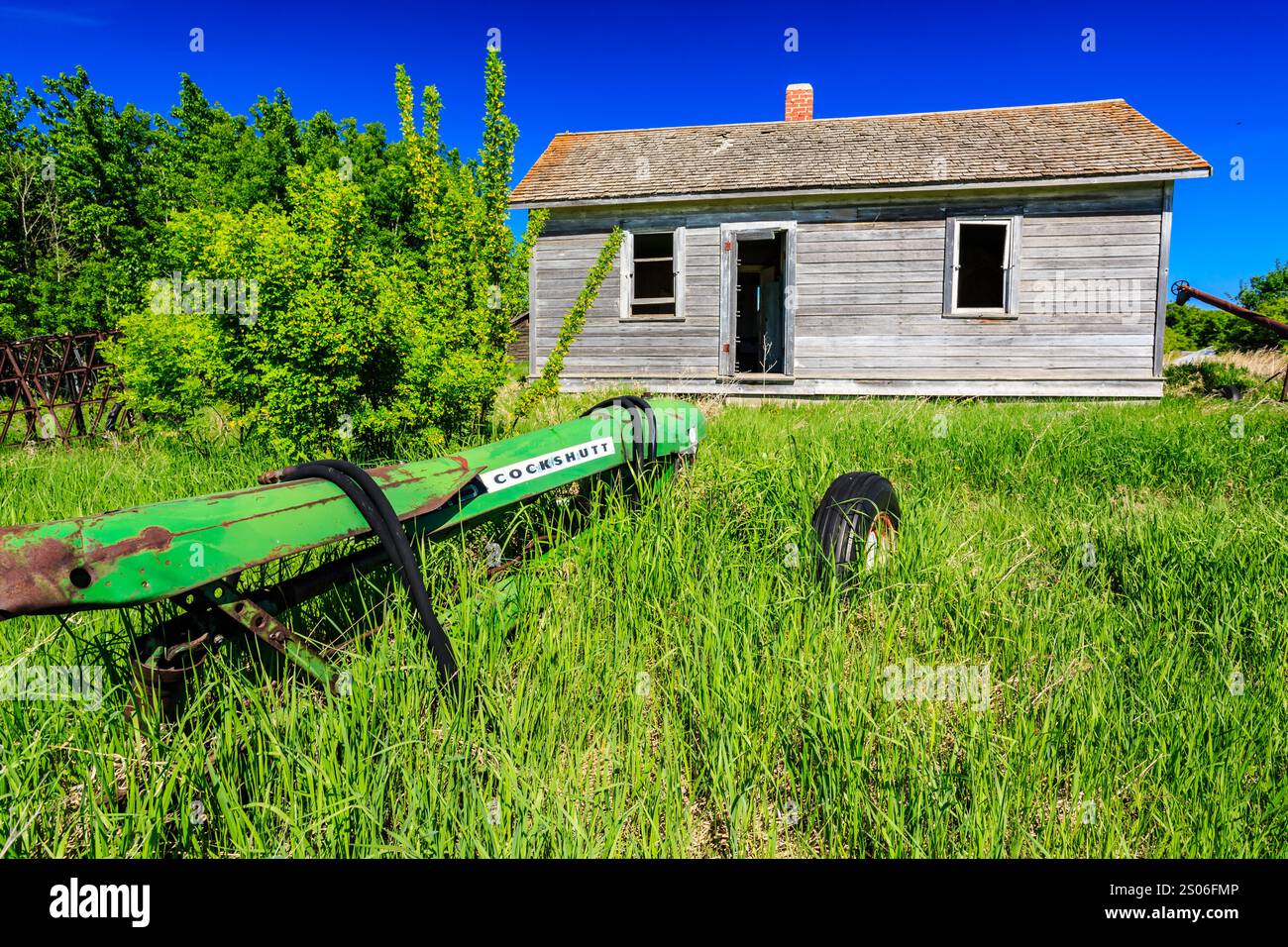 A green tractor is sitting in a field next to a house. The house is old ...