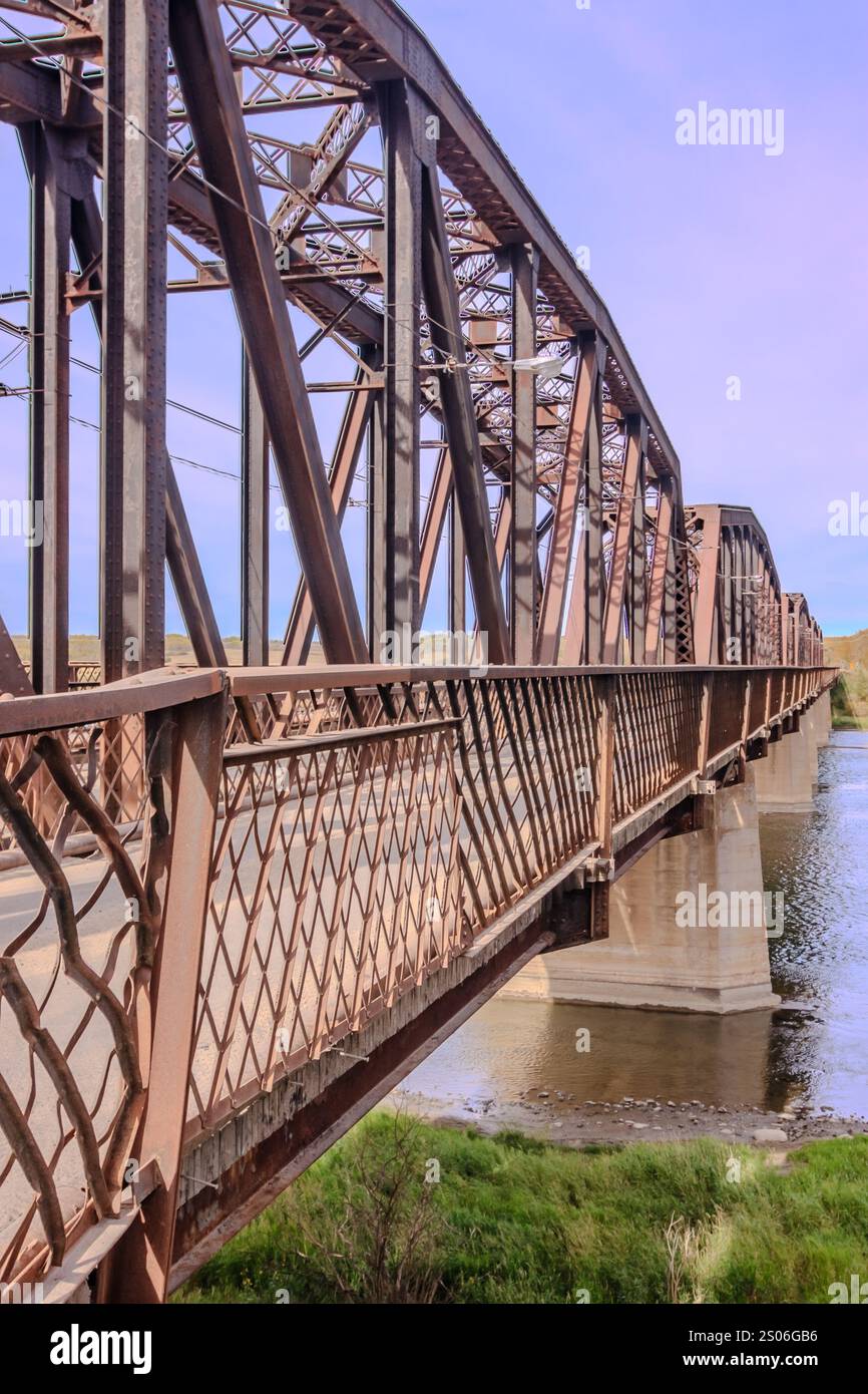 A bridge with a metal railing and a river below. The bridge is old and ...