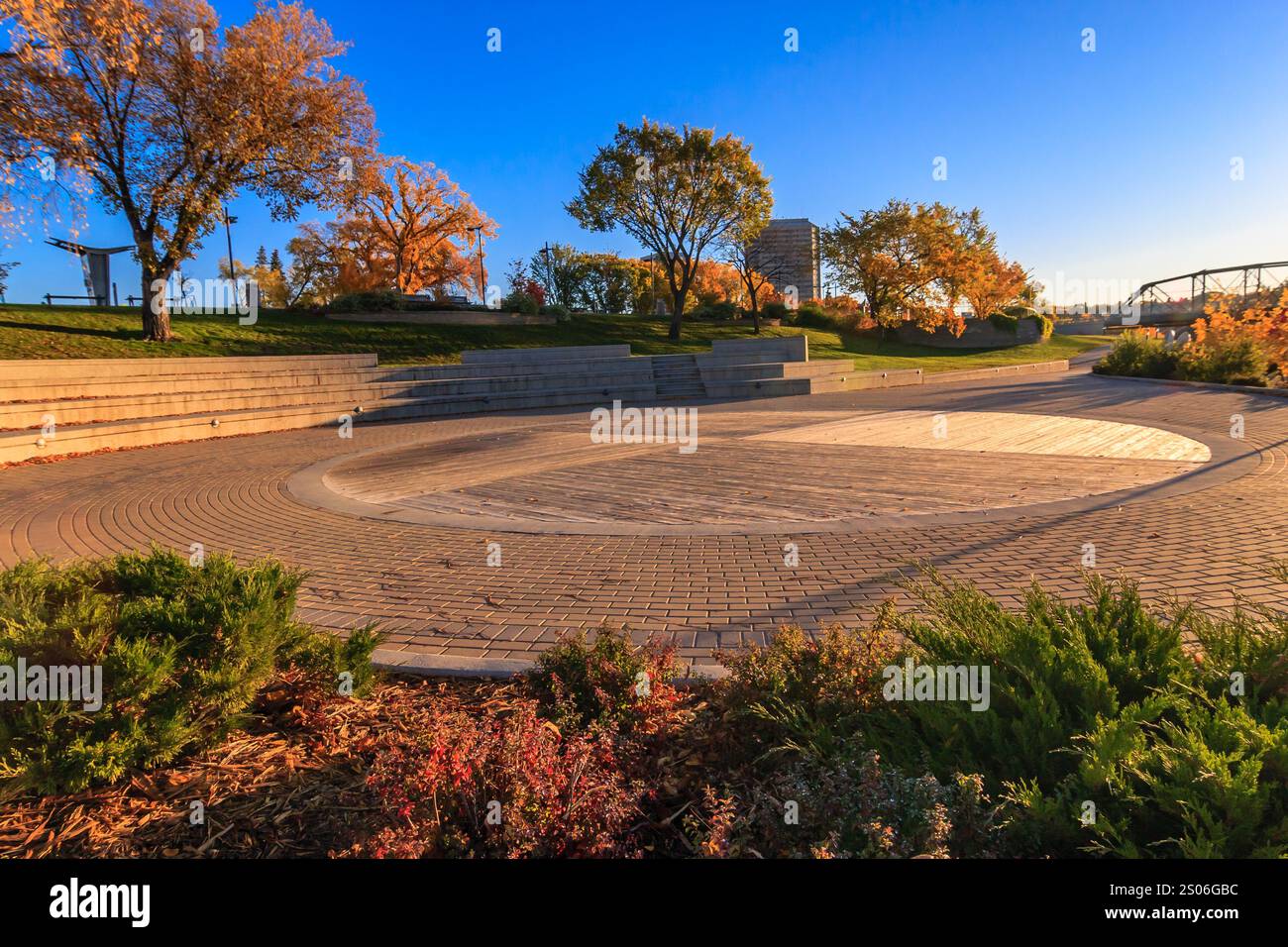A park with a large circular stone area and a few trees. The trees are ...