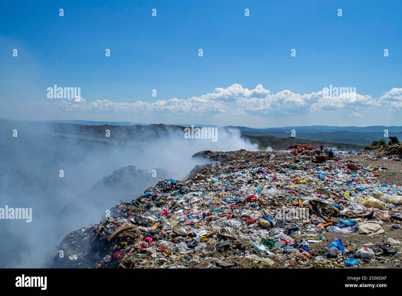 A mountain of trash is on the side of a road. The trash is piled high ...
