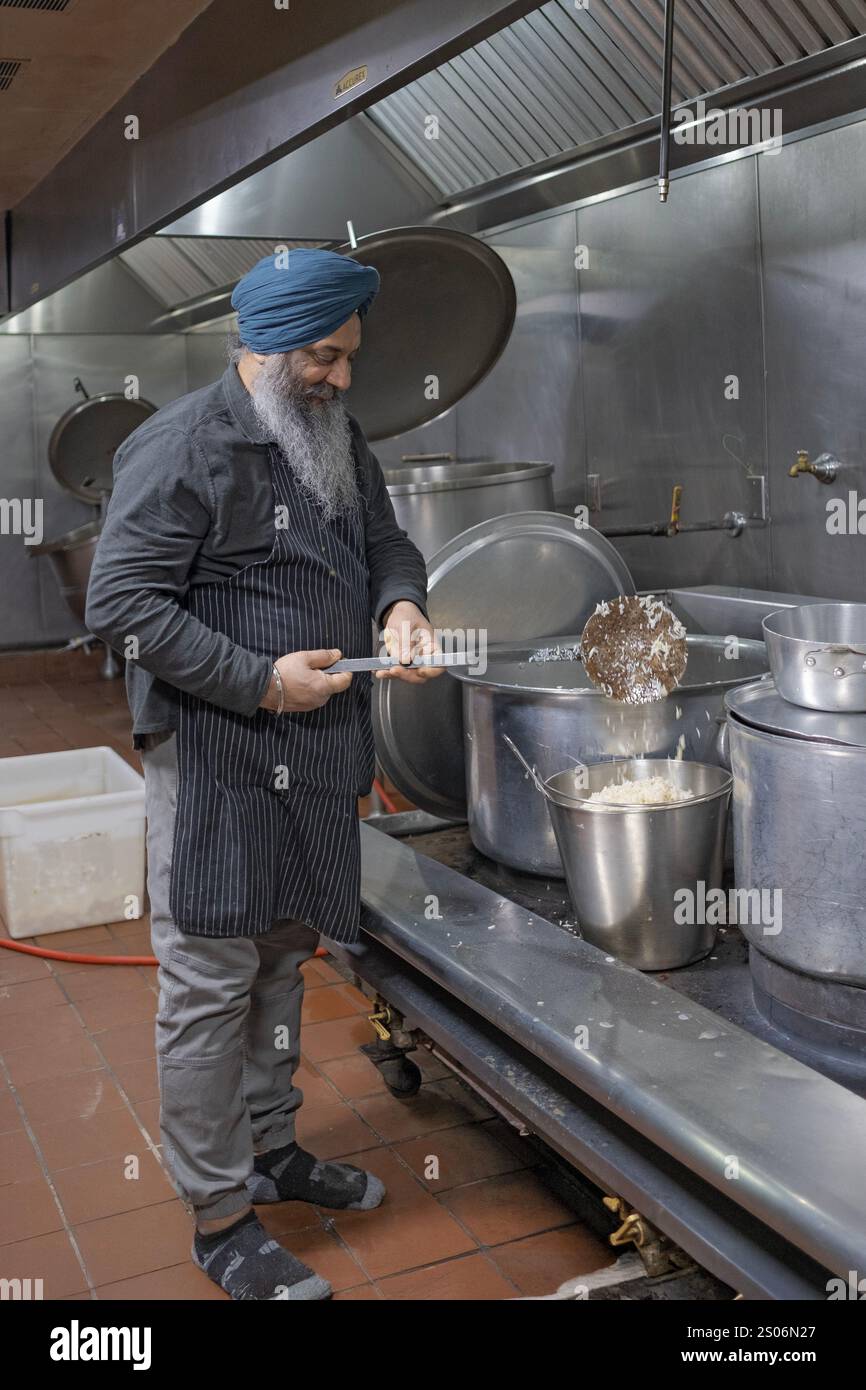 A volunteer in a langar communal kitchen makes rice which will be ...
