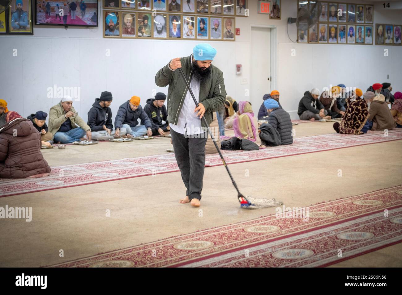 Under rows of photos of Sikh holy men, a volunteer in a blue turban ...