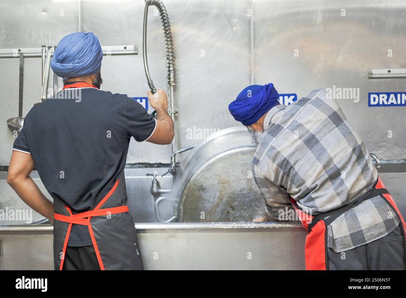 Devout Sikh volunteers wash a huge pot in the langar communal kitchen ...