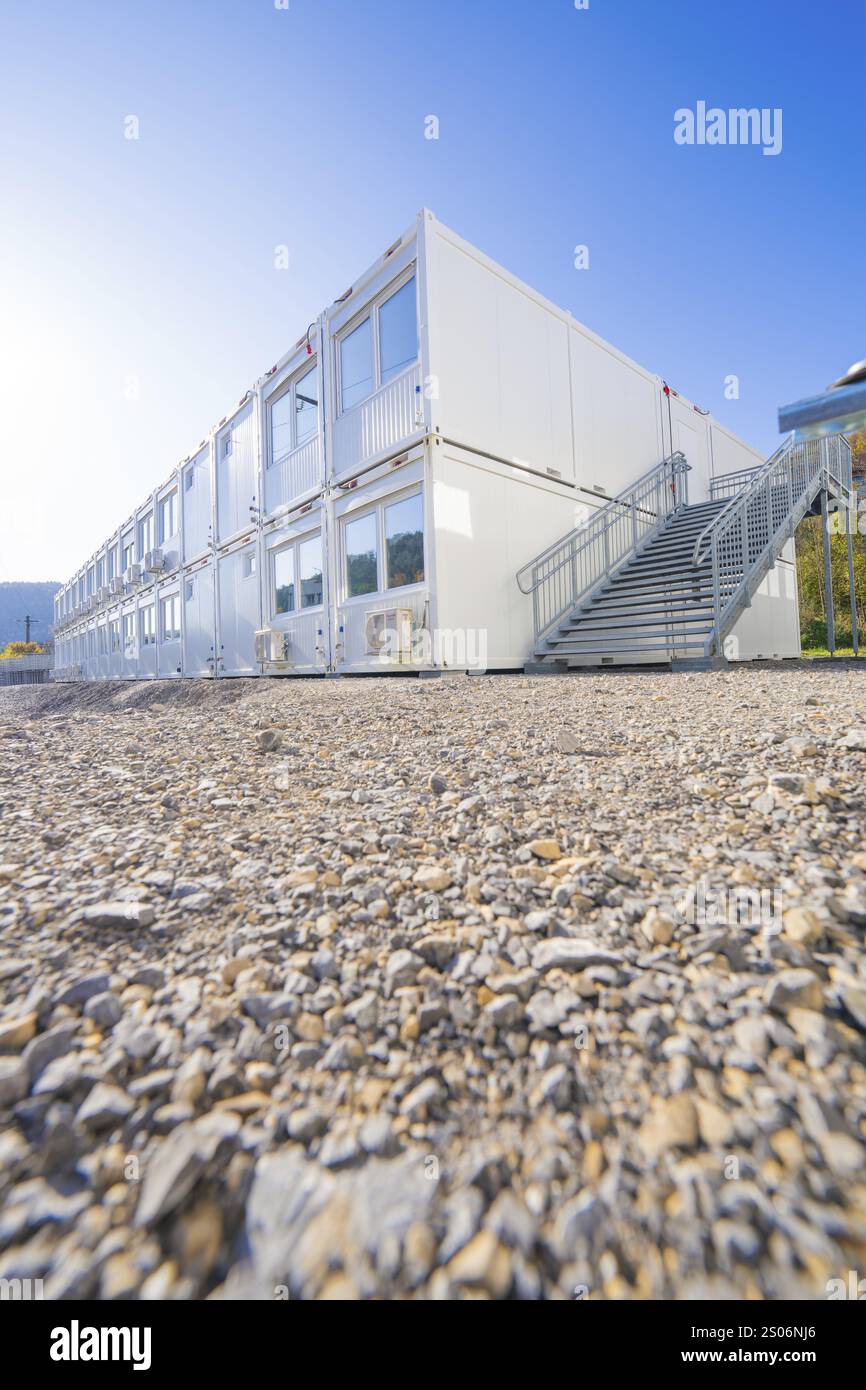 Container building with stairs under blue sky on gravelled ground ...