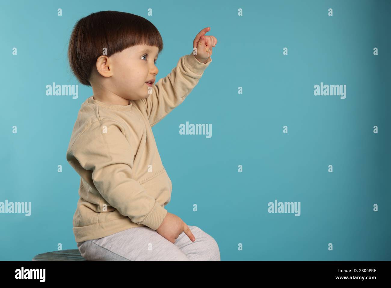 Portrait of cute little boy pointing at something on light blue ...