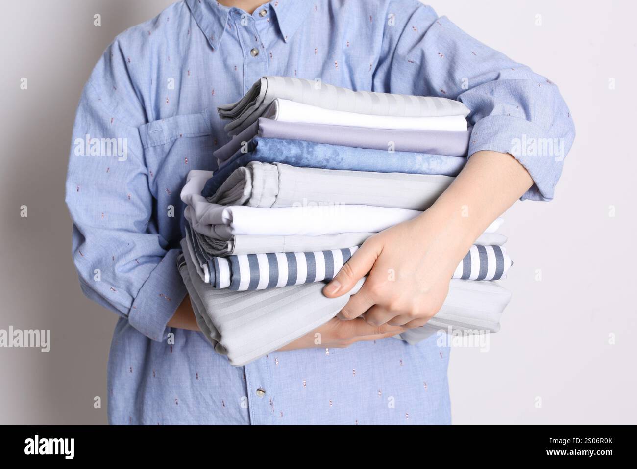 Woman holding stack of clean bed linens on white background, closeup ...