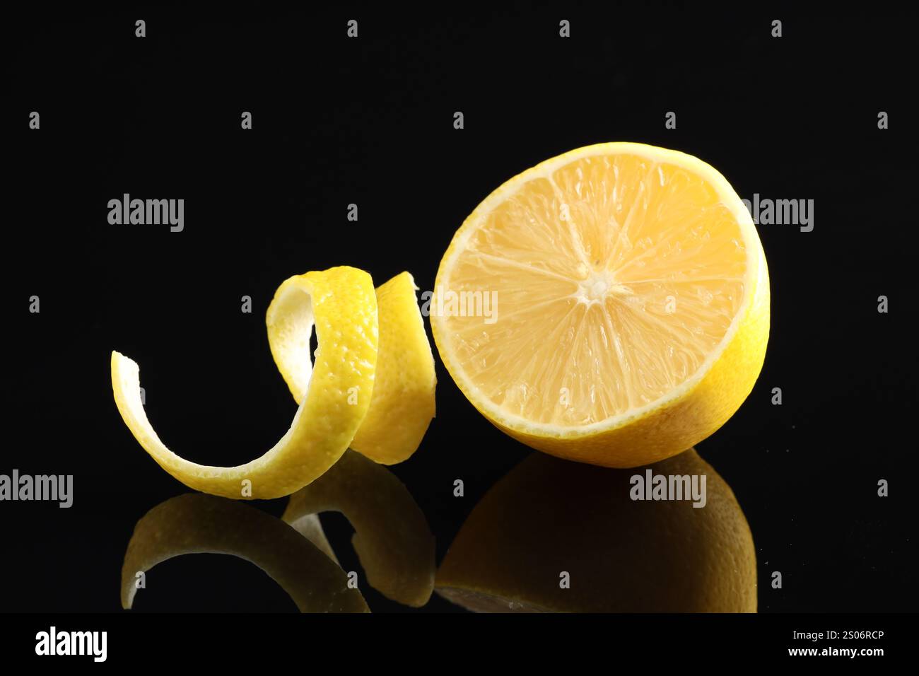 Fresh lemon peel and half of fruit on black glass surface, closeup ...