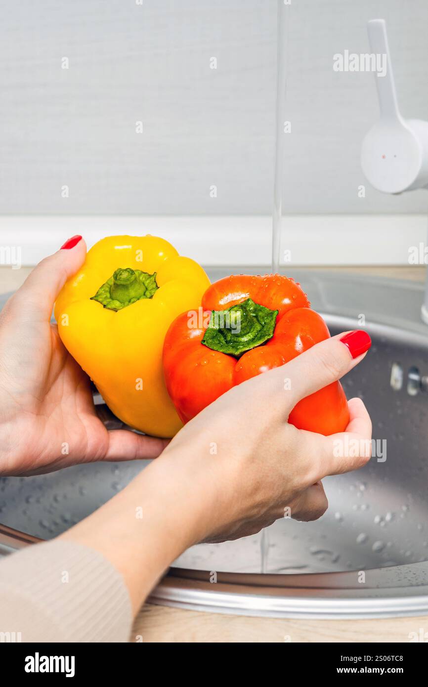 woman washing bell peppers in kitchen sink. housewife washes vegetables ...