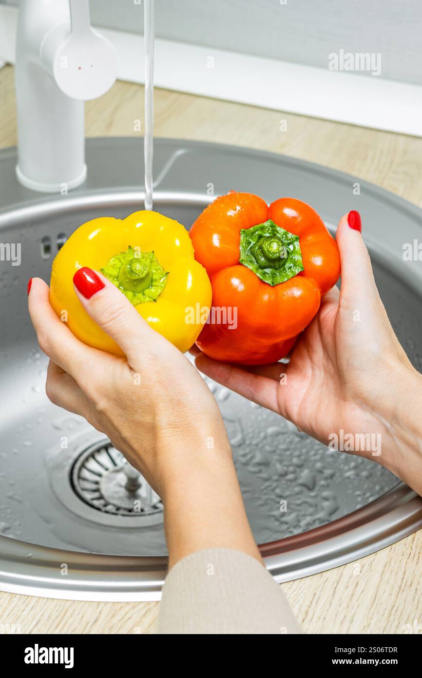 woman washing bell peppers in kitchen sink. housewife washes vegetables ...