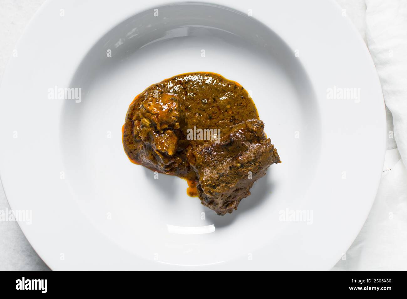 Overhead view of Nigerian banga soup with fish and beef in a white ...