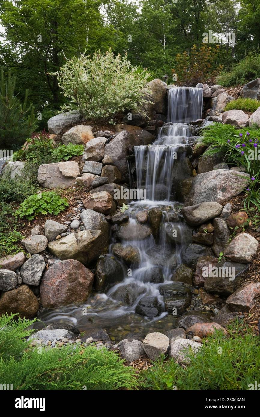 Cascading waterfall through rock edged borders with perennial plants ...