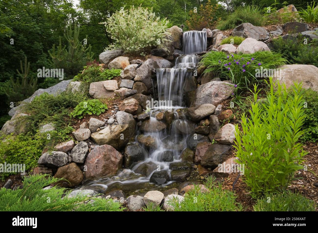 Cascading waterfall through rock edged borders with perennial plants ...