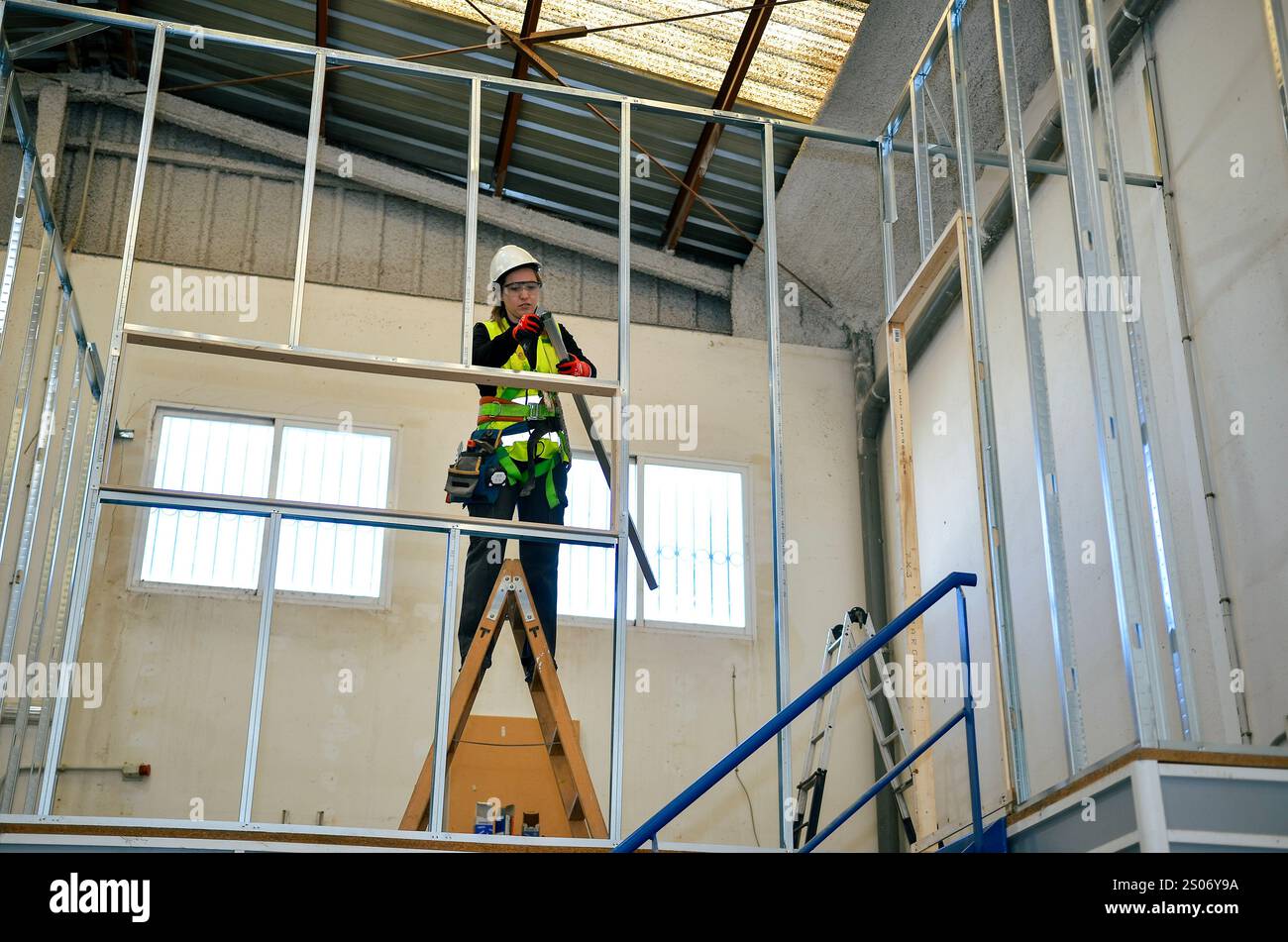 Female construction worker mounting plasterboard on metal frame on ...