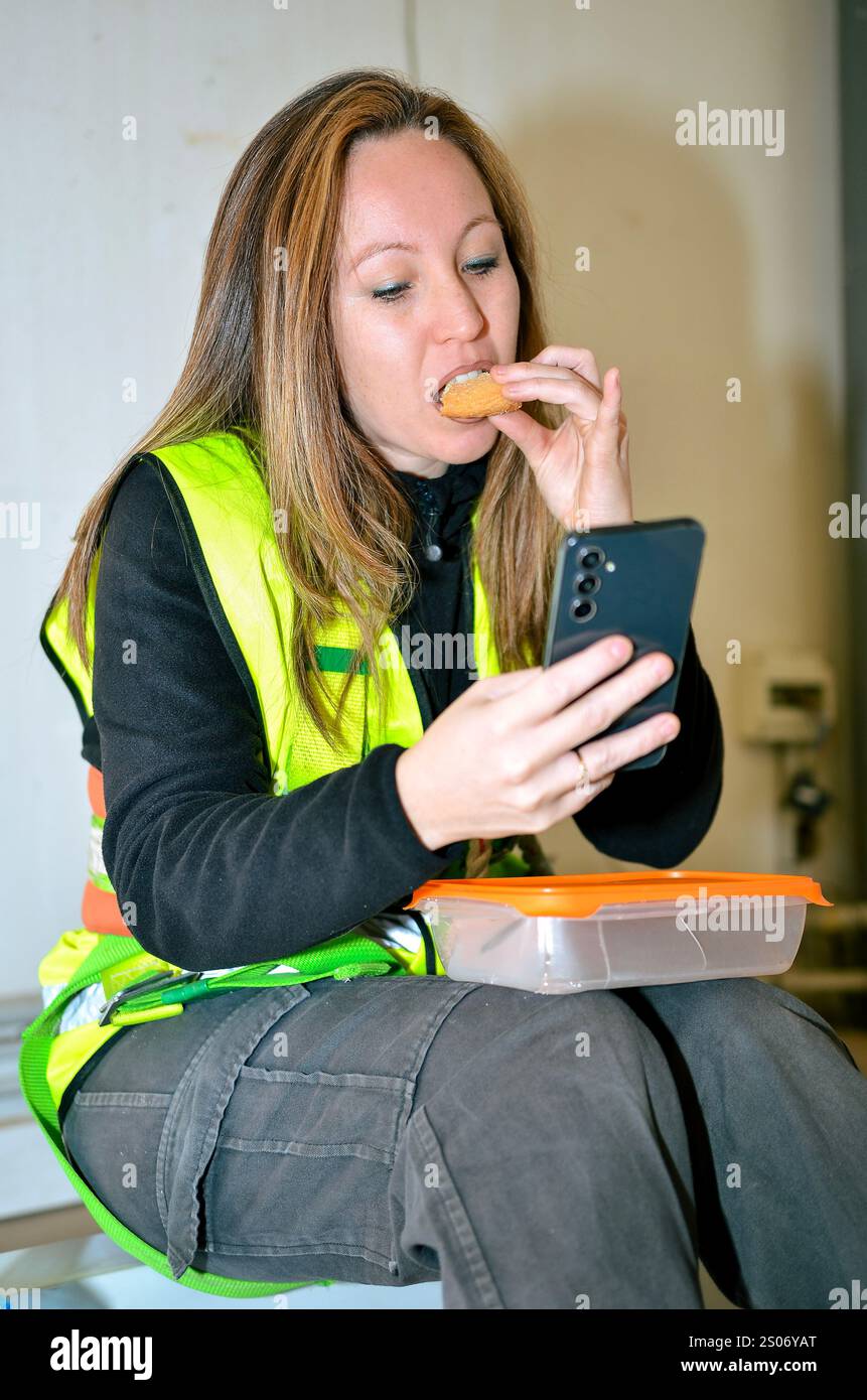 Female construction worker taking a lunch break, eating a snack and ...