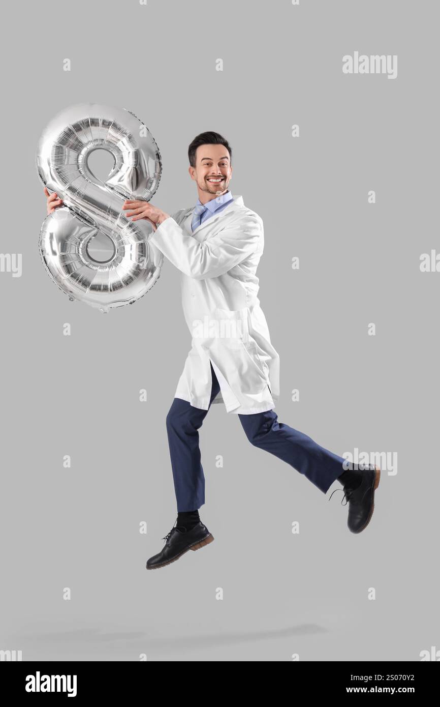 Male doctor with balloon in shape of figure 8 jumping on grey ...