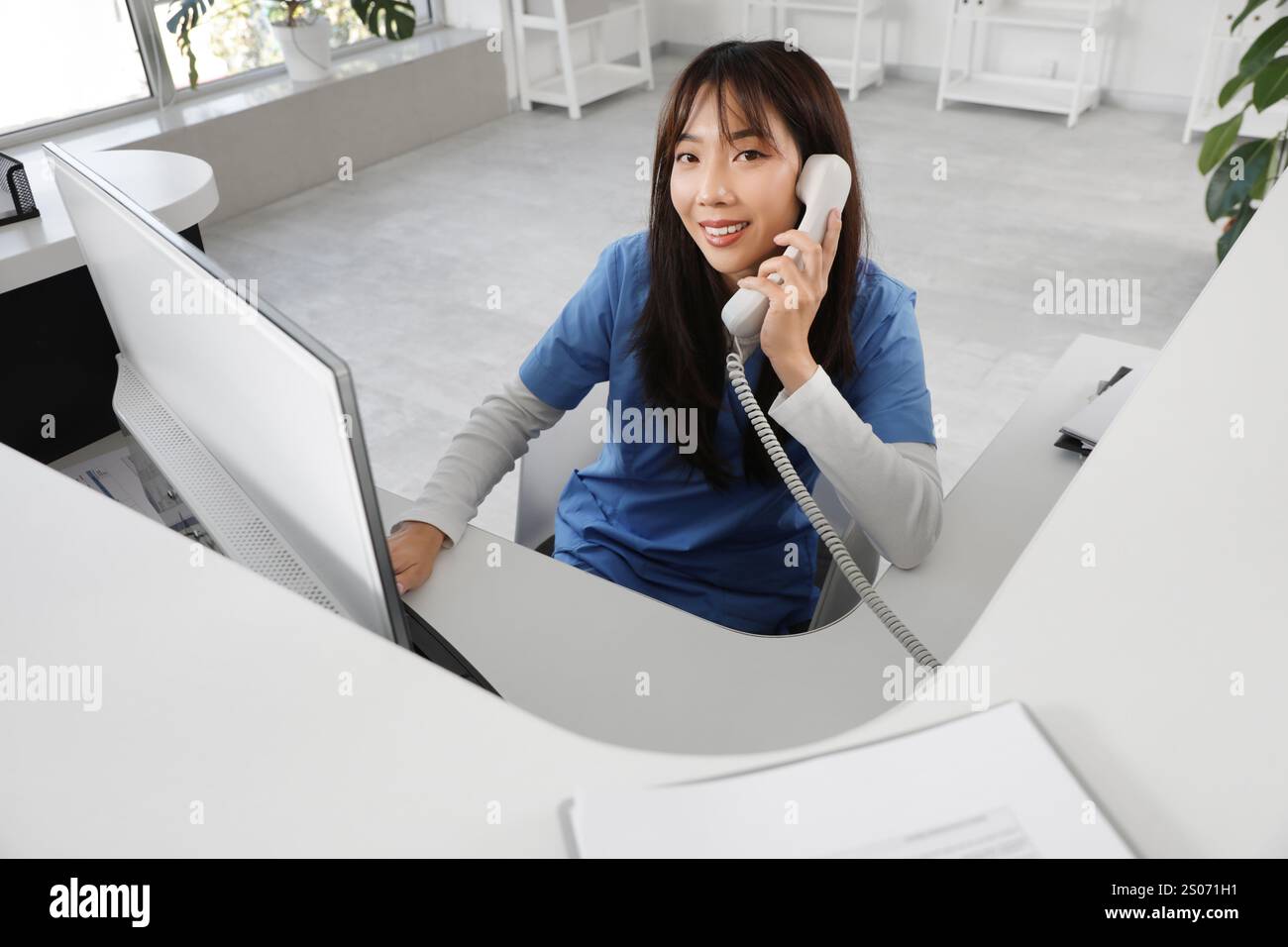 Female Asian medical intern talking by telephone at reception in clinic ...