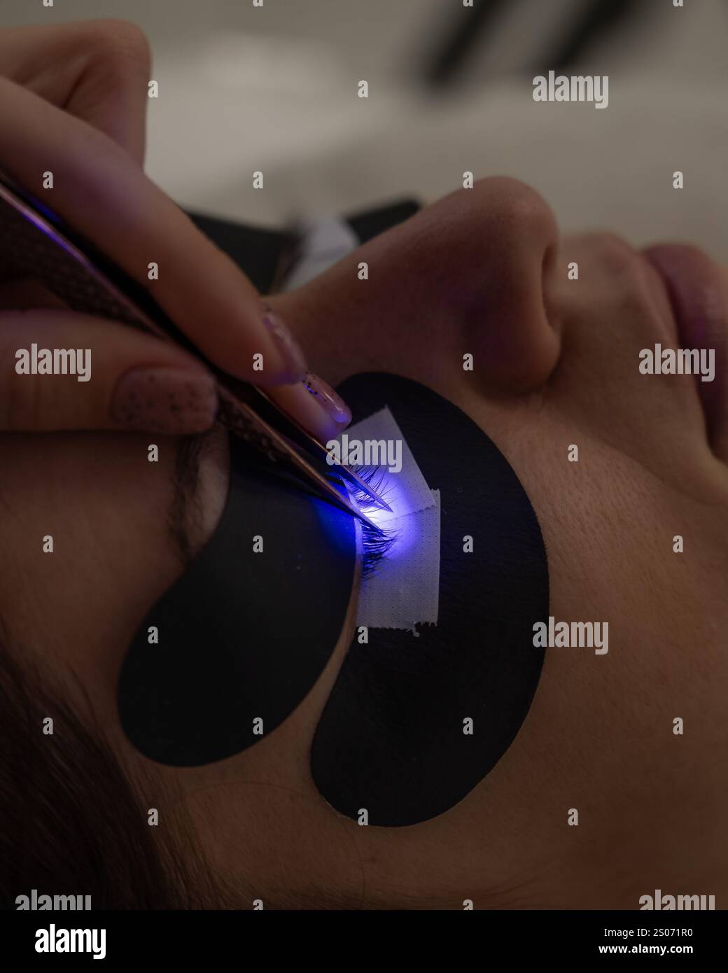A woman undergoing eyelash extension procedure using an ultraviolet ...