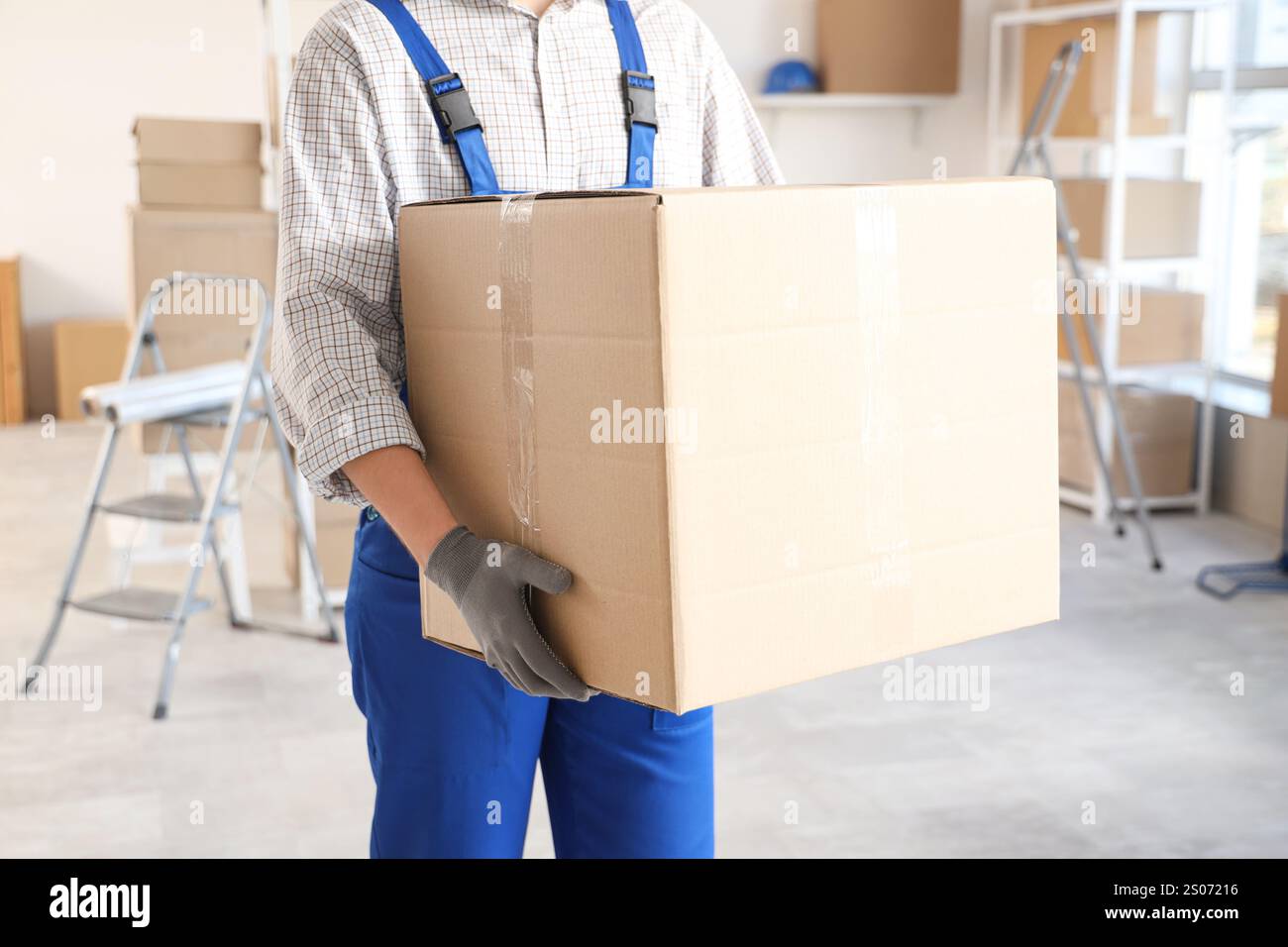 Male loader carrying cardboard box in warehouse Stock Photo - Alamy