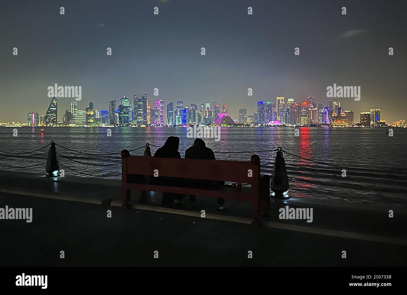 People seen sitting on a bench on the seaside promenade of Doha Stock ...