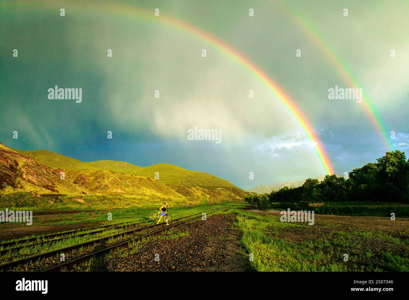 Rainbow over female mountain biker carrying her bike over railroad ...