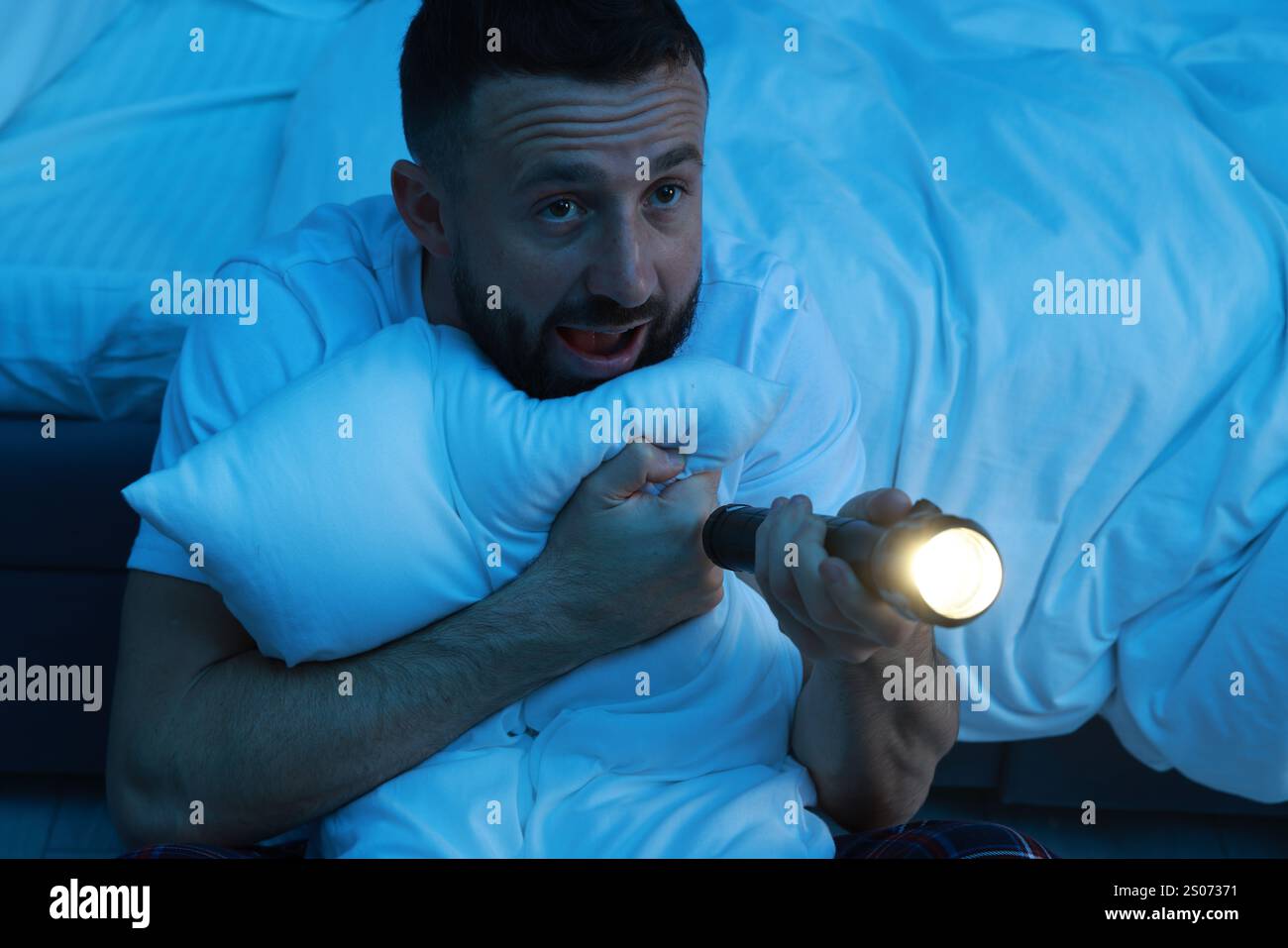Fear of darkness. Scared man with flashlight hugging pillow in bedroom ...