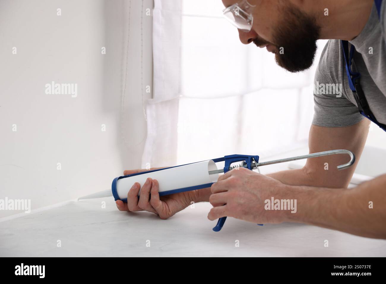 Man with caulking gun sealing countertop indoors Stock Photo - Alamy