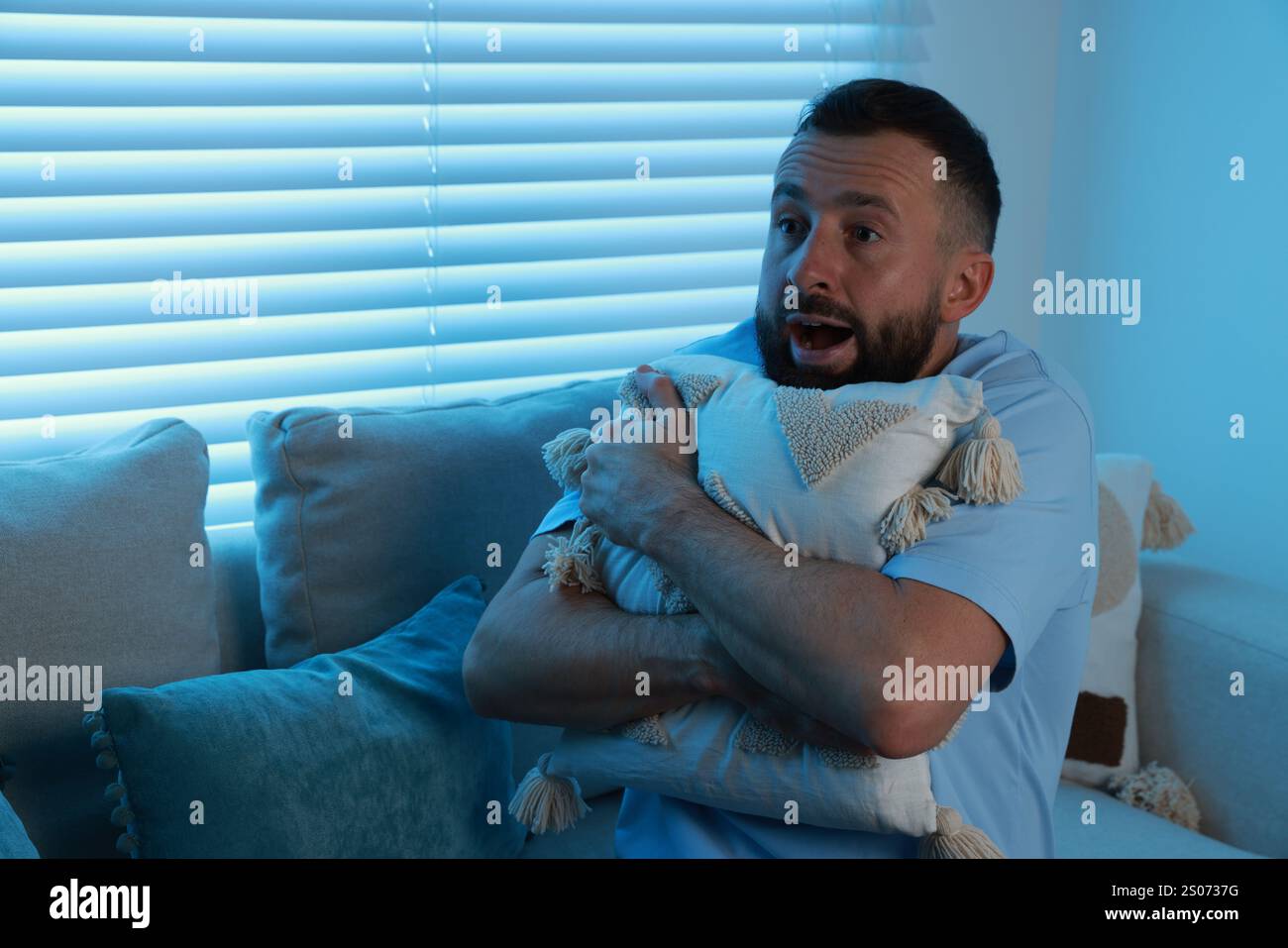 Fear of darkness. Scared man hugging pillow on couch in dark room Stock ...