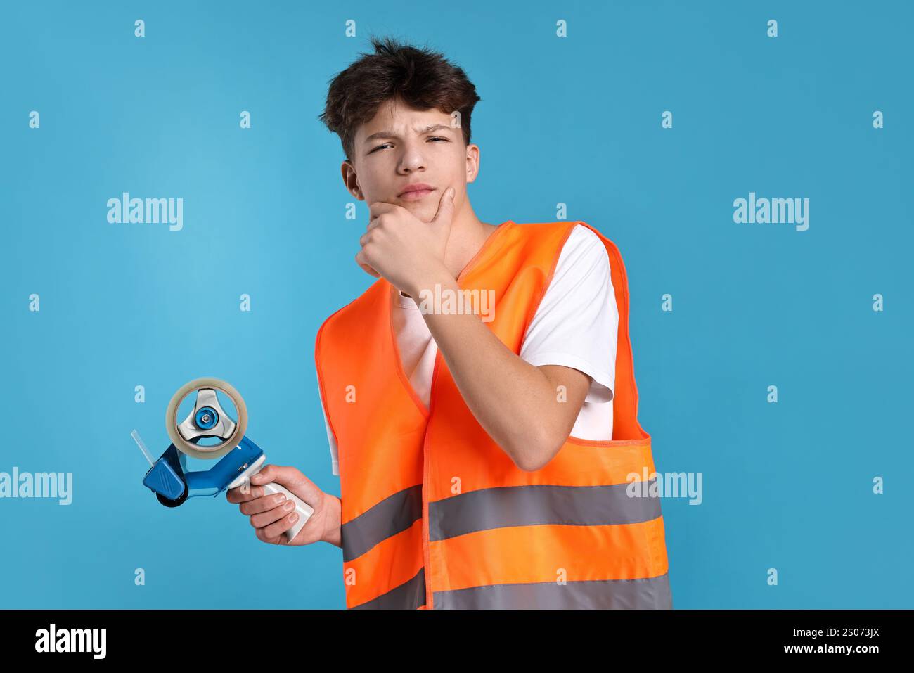 Teenage boy with tape gun dispenser in safety vest working as warehouse ...