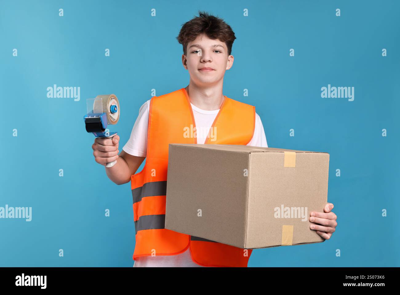 Teenage boy with tape gun dispenser and box in safety vest working as ...