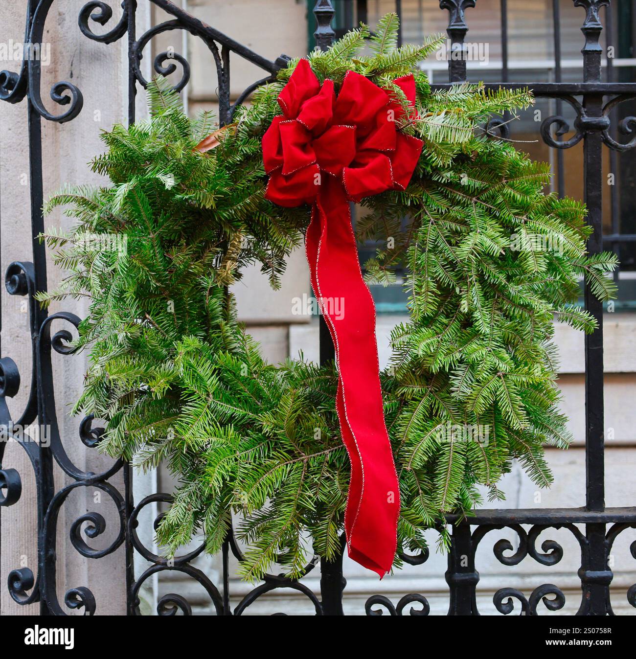 Decorative pine wreath with bright red bow on an exterior metal gate ...