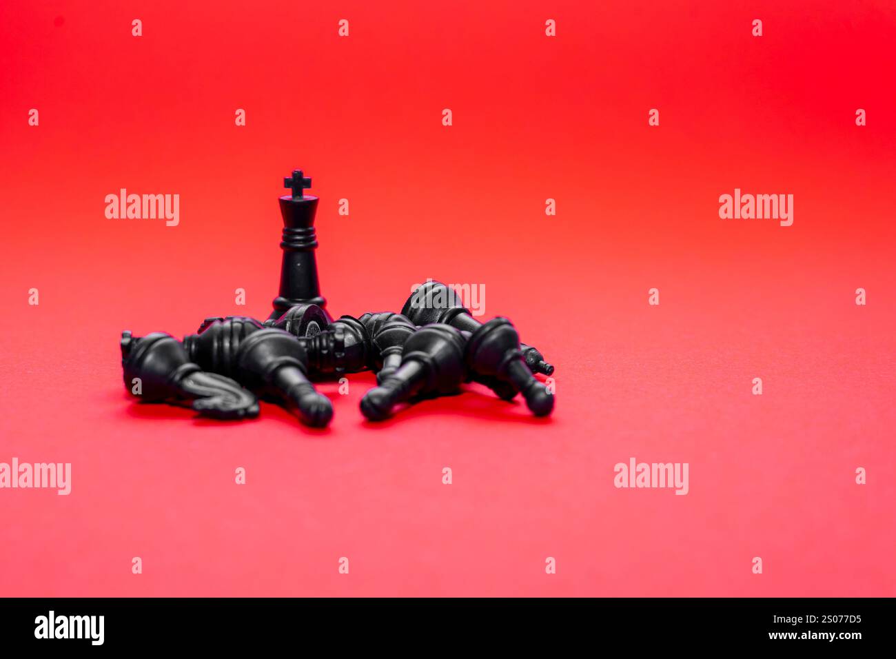 A group of black chess pieces lies scattered around a king piece. The ...