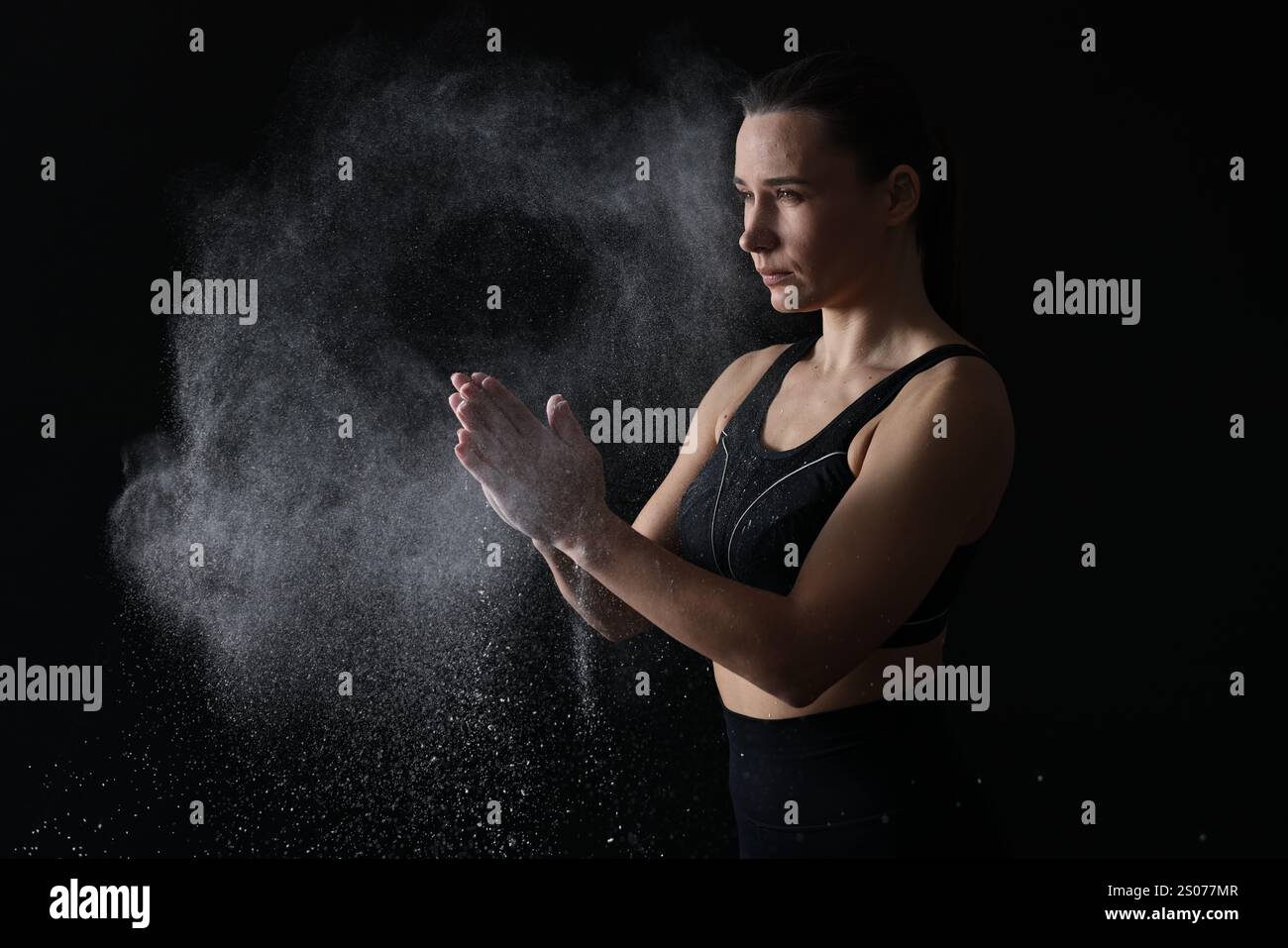 Woman clapping hands with talcum powder before training on black ...