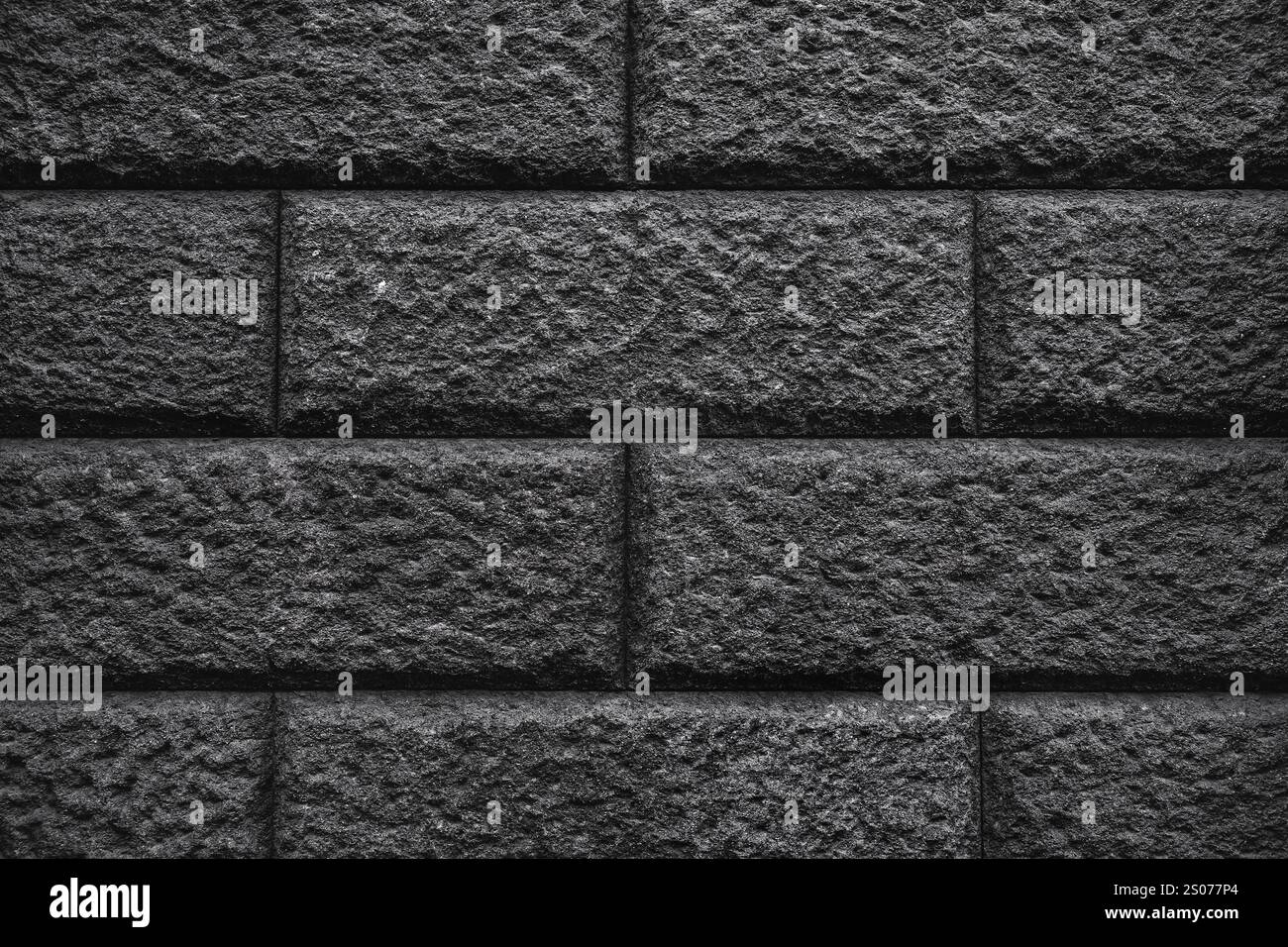 A textured wall of dark gray bricks, with a rough and uneven surface ...
